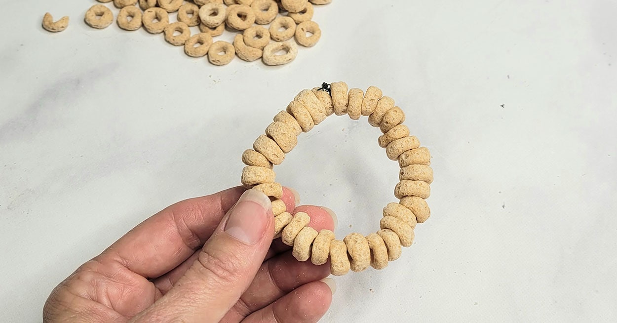 A hand holding a circle of round cereal on a floral wire.