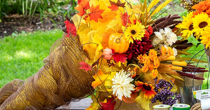 A cornucopia-shaped wreath with fall leaves, pumpkins and sunflowers