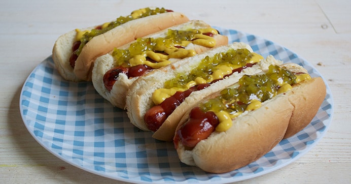 FFour hot dogs in buns with mustard, ketchup and relish on a blue and ...