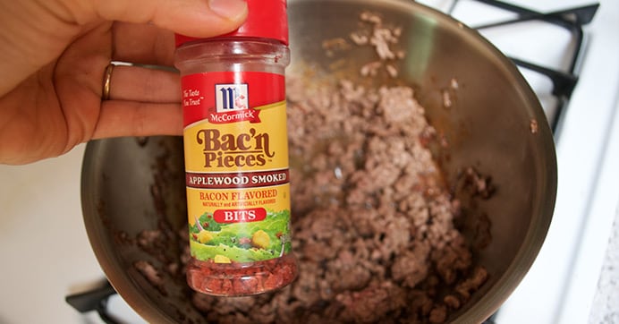 A hand holding a bottle of bacon bits with cooked ground beef in the ...