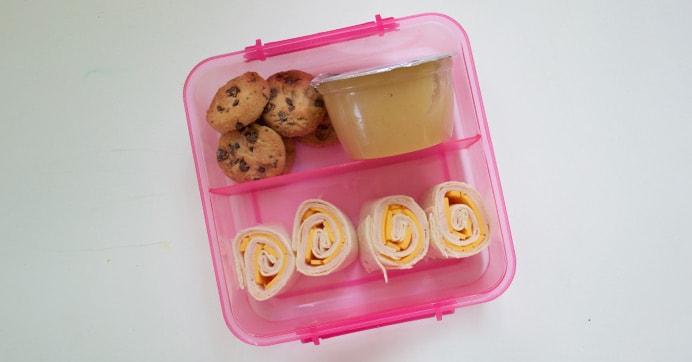 A divided pink container with applesauce, cookies and sandwich ...
