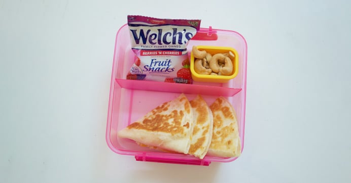 A pink divided container with quesadilla triangles, a bag of fruit ...