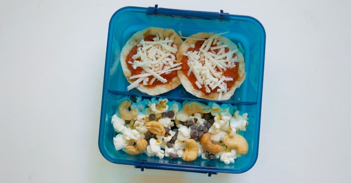 A blue divided container with mini pizzas and a popcorn snack in it.