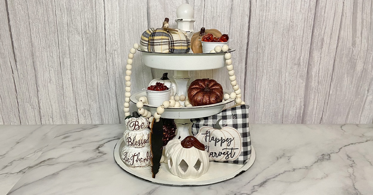 Rustic white tiered tray decorated with a variety of fall-themed items.