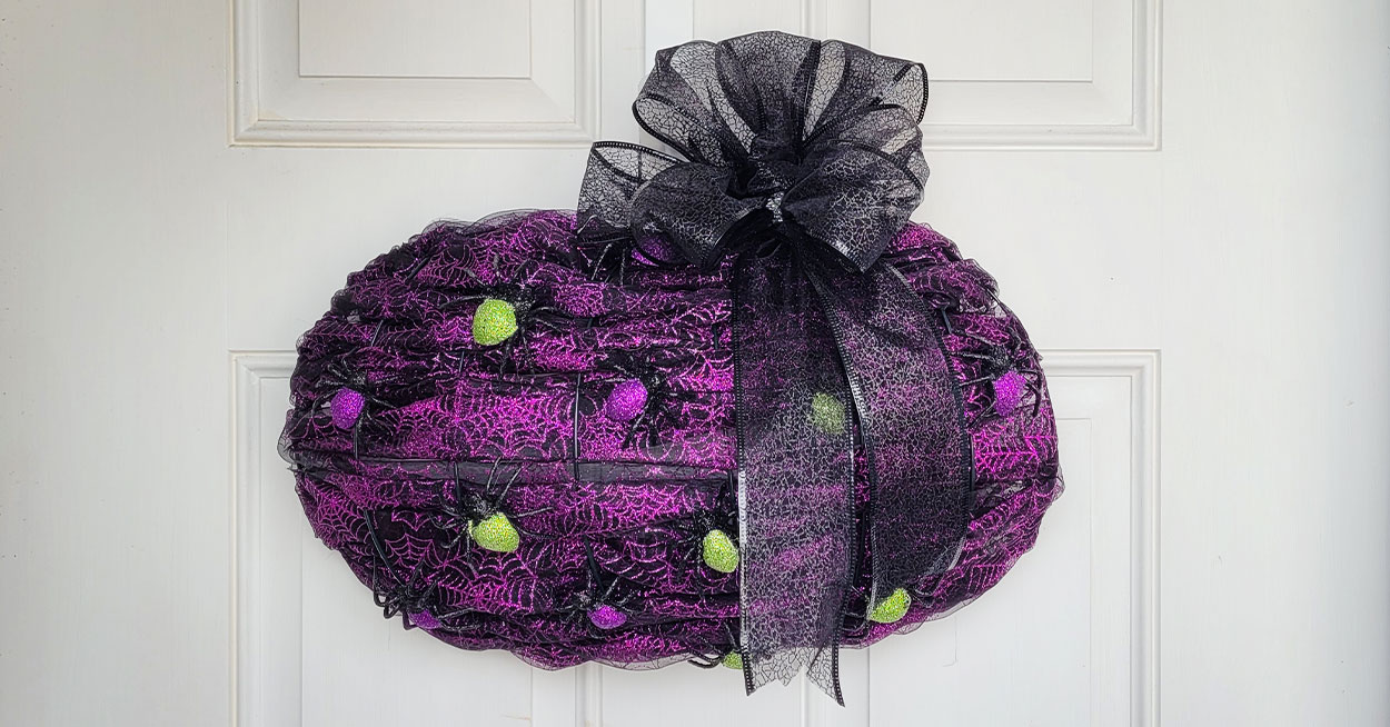 A pumpkin-shaped wreath decorated with purple and black spider web ...