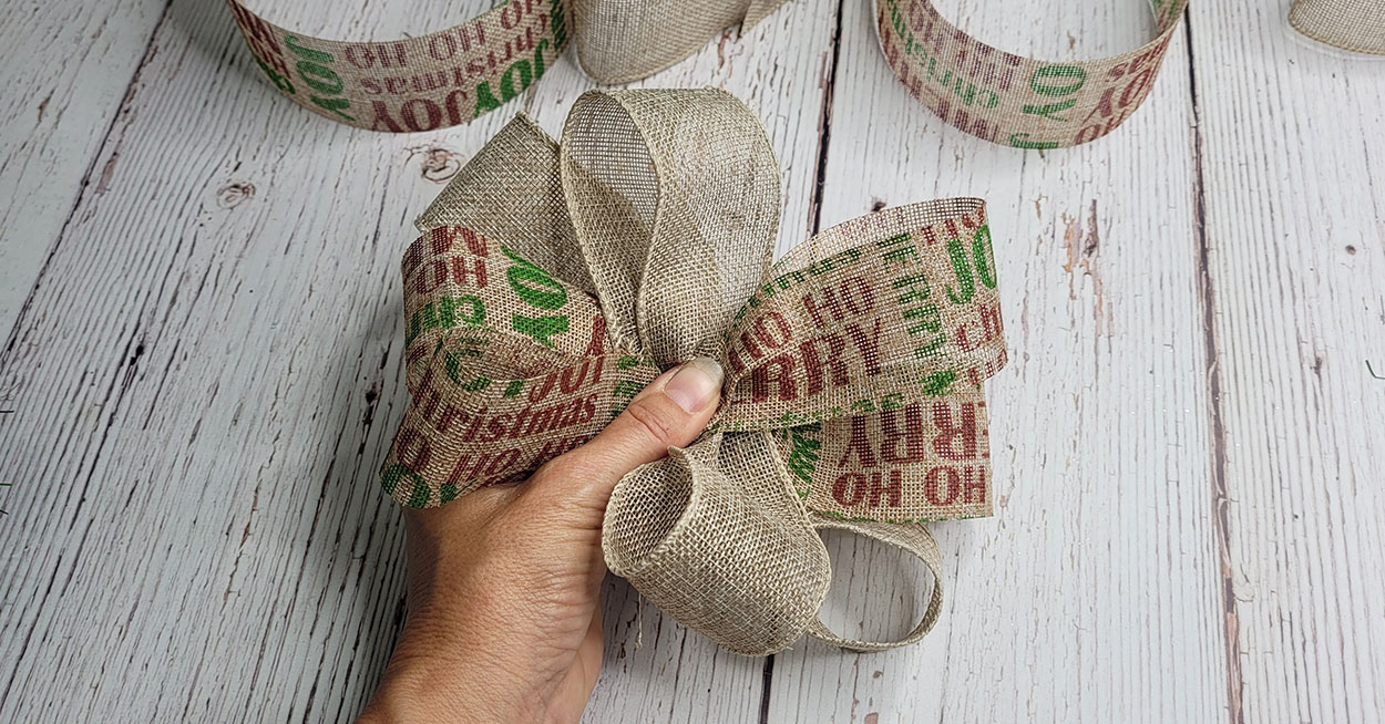 hand holding a bow made out of burlap and Christmas ribbon