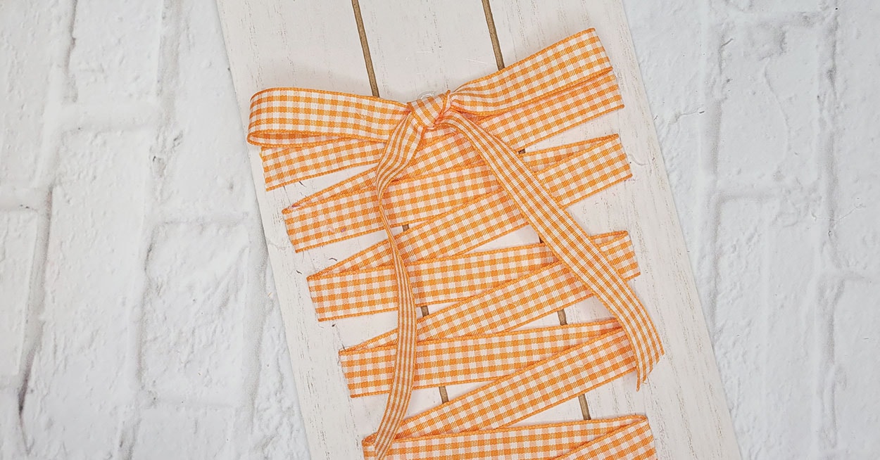 Wooden plank with orange and white ribbon in a zig zag pattern.