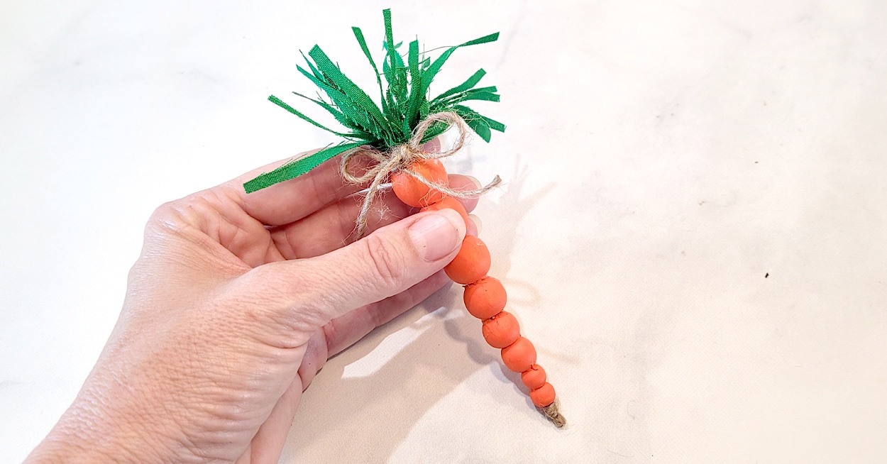 A hand holding a carrot made from wooden beads.