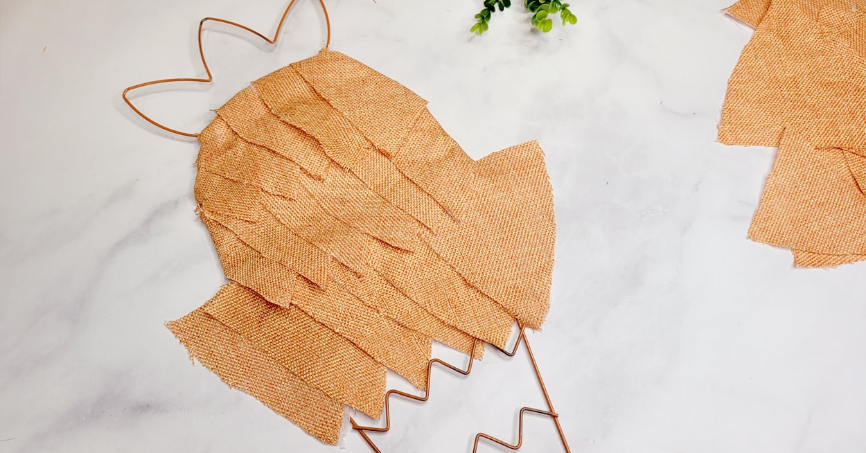 An orange wire carrot with pieces of material glued on it.