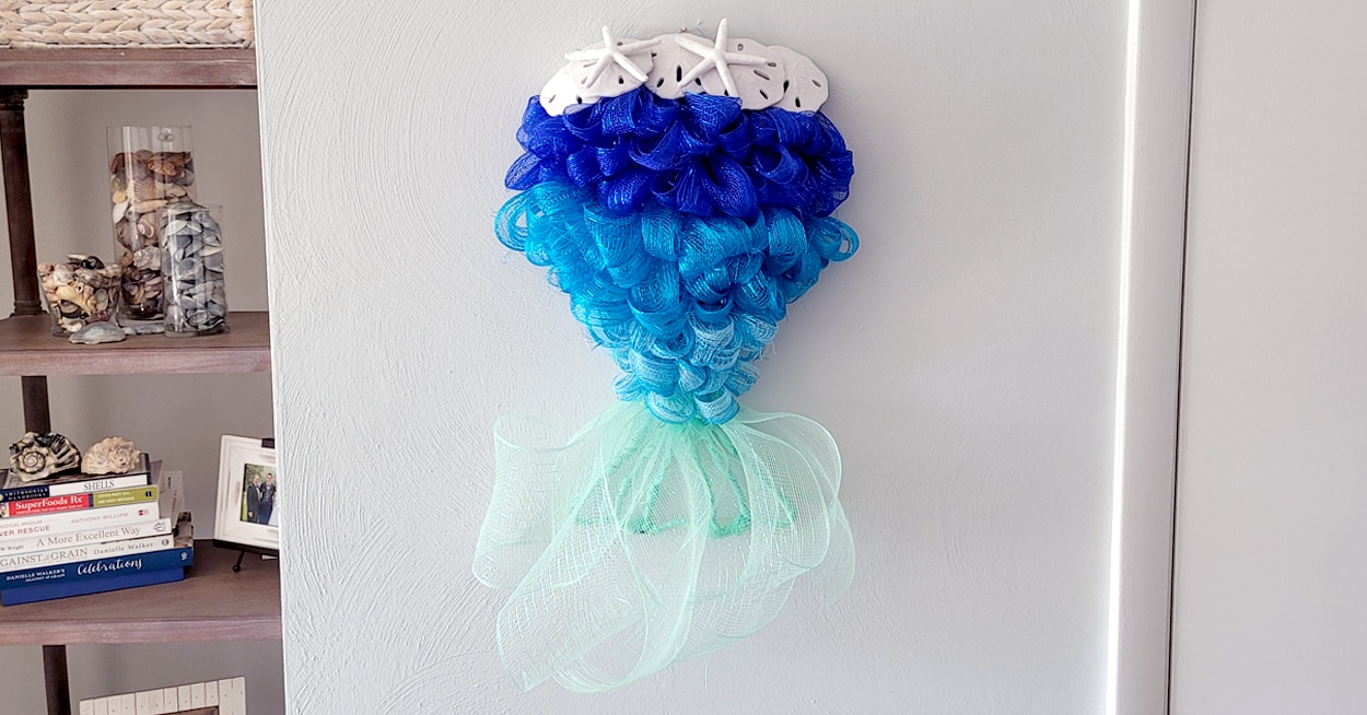 A summer wreath that looks like a mermaid tail on a white front door.