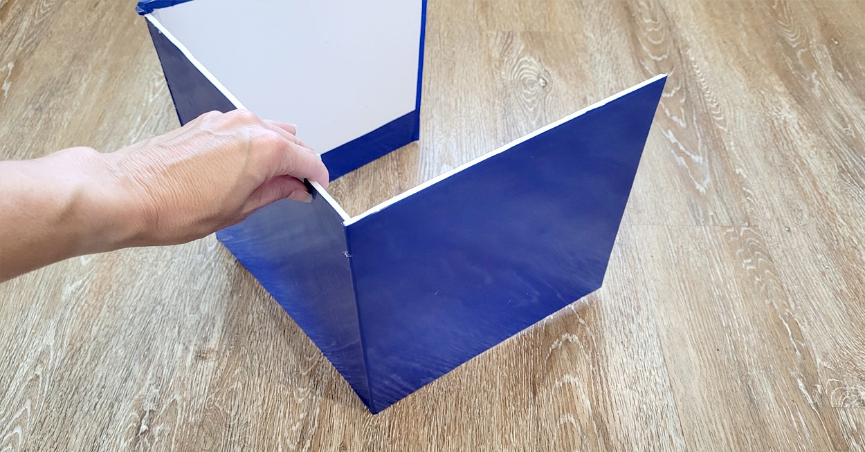 A hand holding foam board covered in blue to form a box.