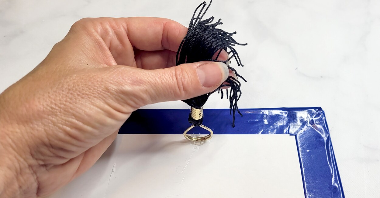 A hand holding a keychain tassel on a piece of foam board.
