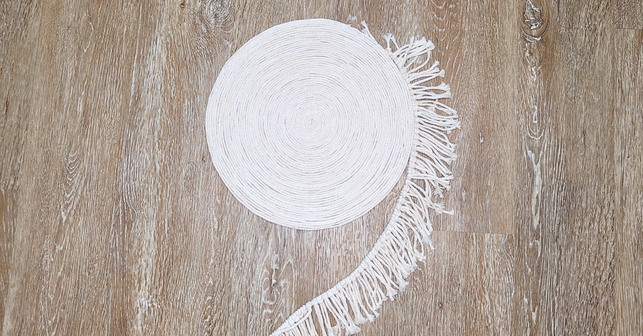 A round piece of foam board covered in macrame cotton twine with some ...