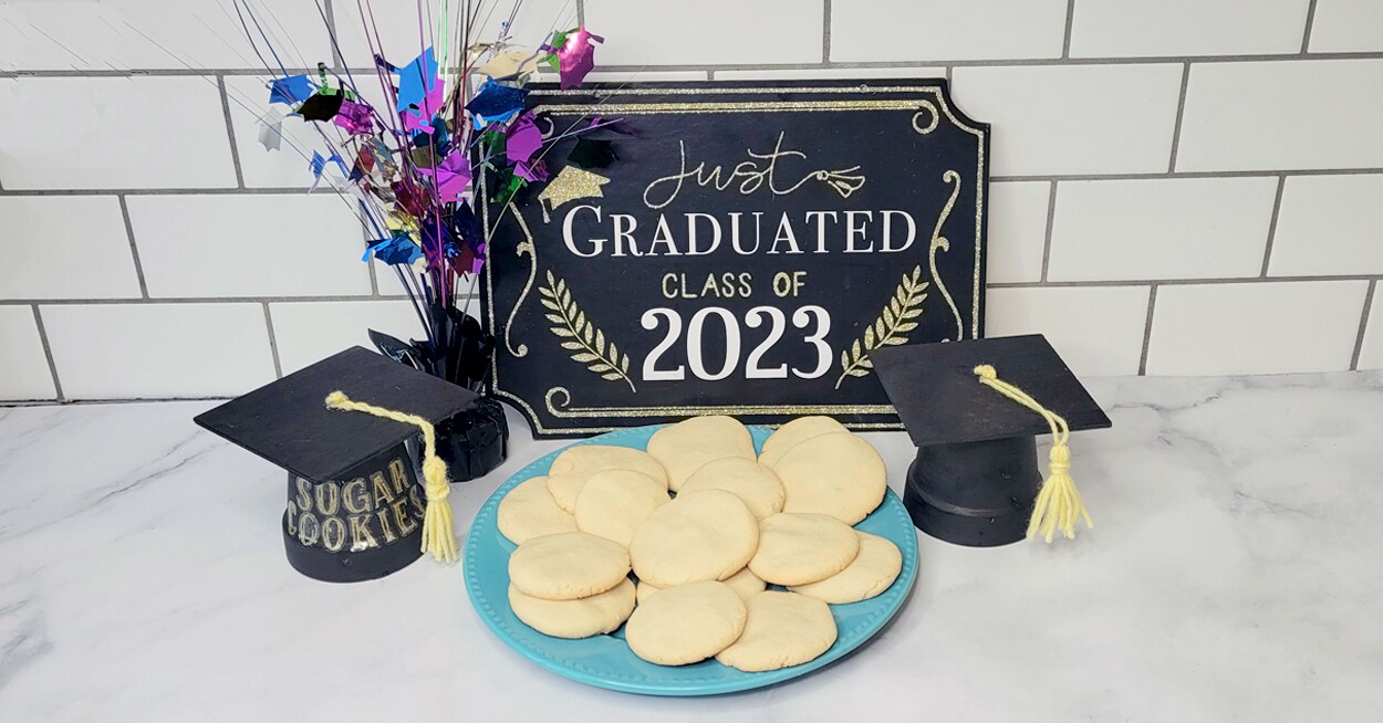 A graduation sign, a plate of cookies, two small grad hats.