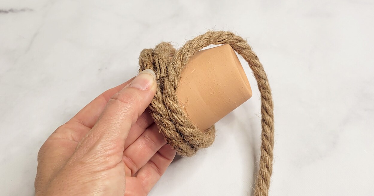 A Small Clay Pot With Nautical Rope On It And A Hand Holding The Pot