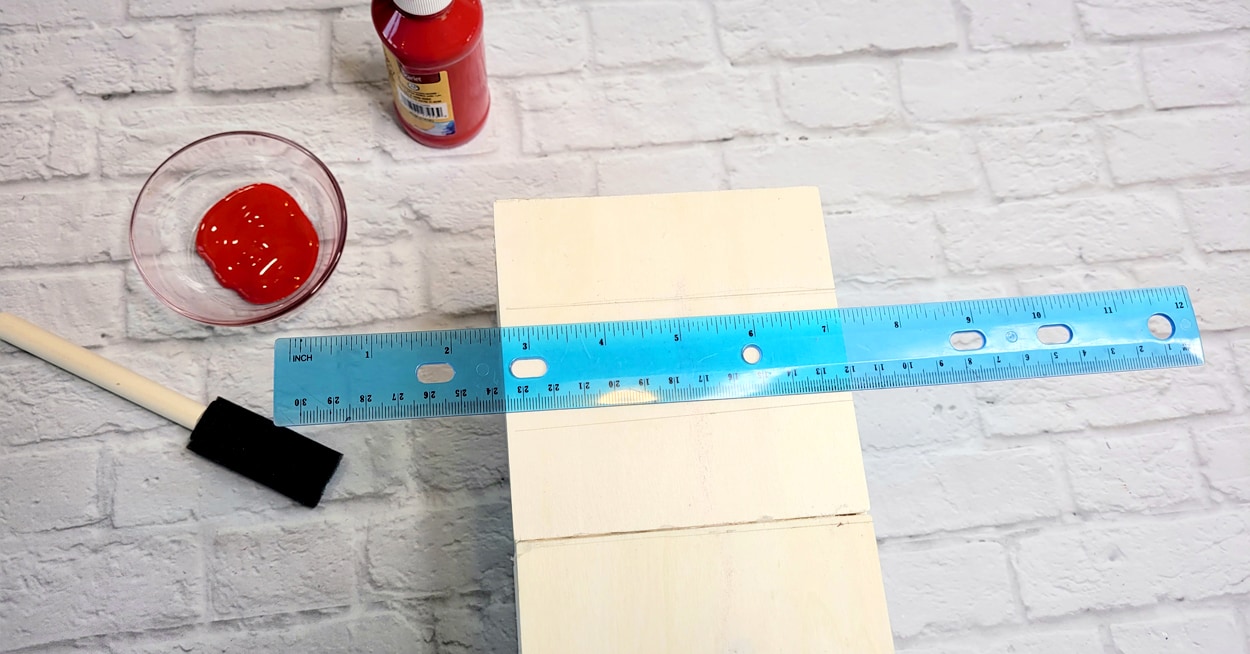 Sponge brush, red paint, and a wooden box with a ruler on it.