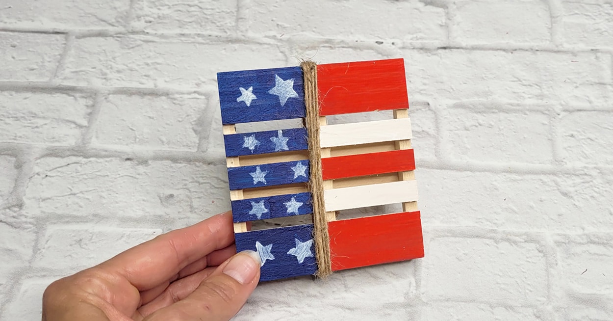 A hand holding a small wooden pallet painted red, white, and blue.