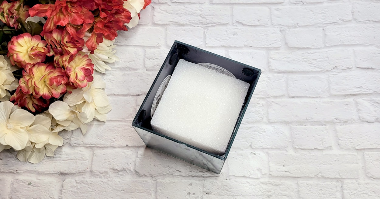 A mirrored box with floral foam in it and flowers.