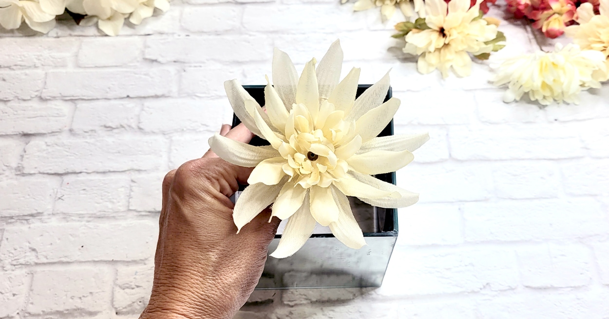 A hand holding a cream flower over a mirrored flower box.