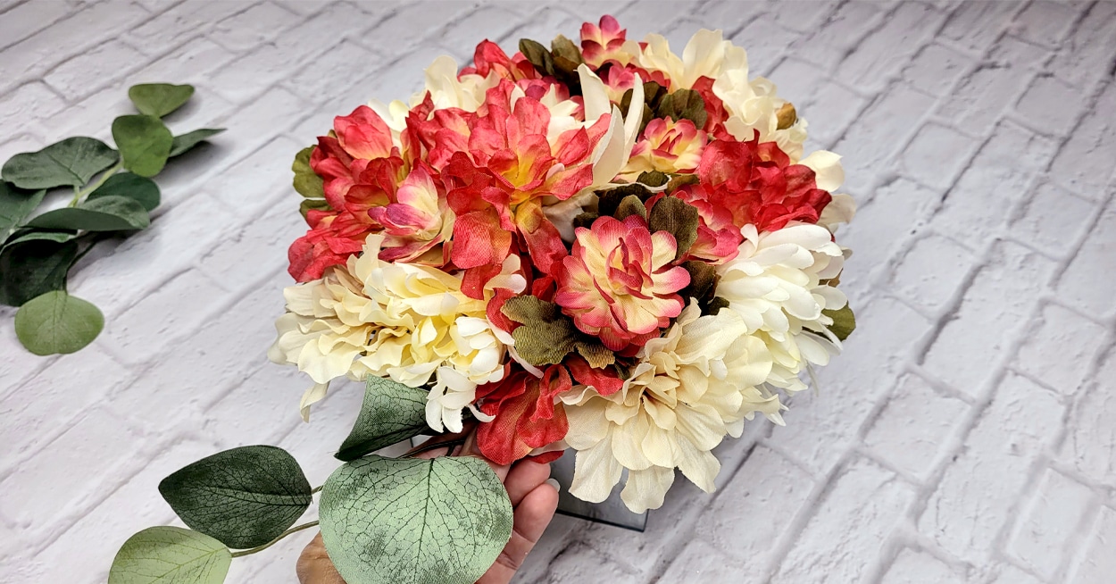 A flower arrangement with a hand holding some greenery.