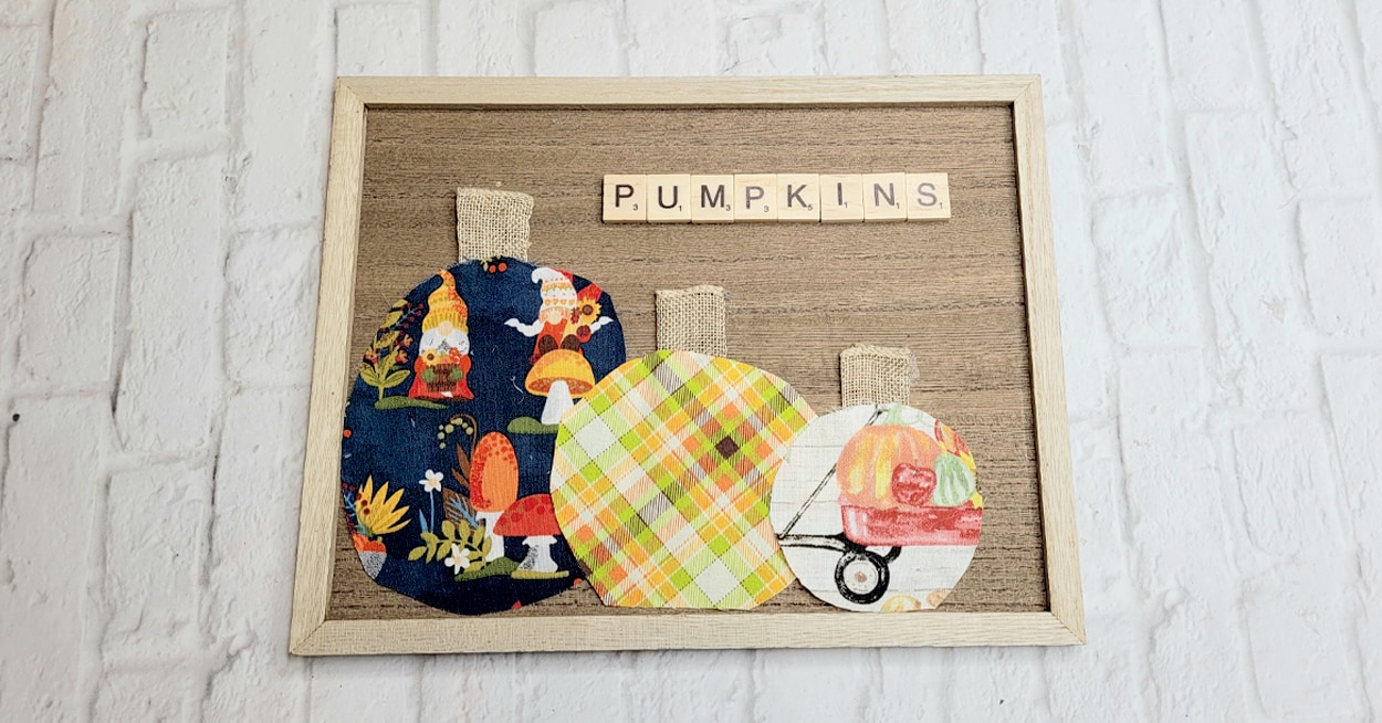 A wooden frame with pieces of fabric shaped like pumpkins on it and ...