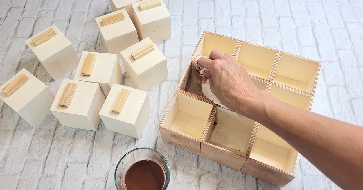 Small wooden boxes, a bowl of paint, and a hand wiping paint on.