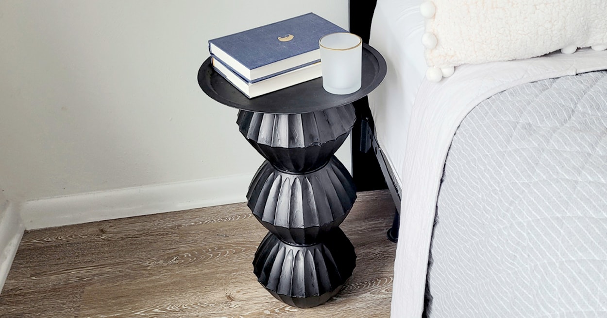 A black side table with books and a candleholder on it next to a bed.