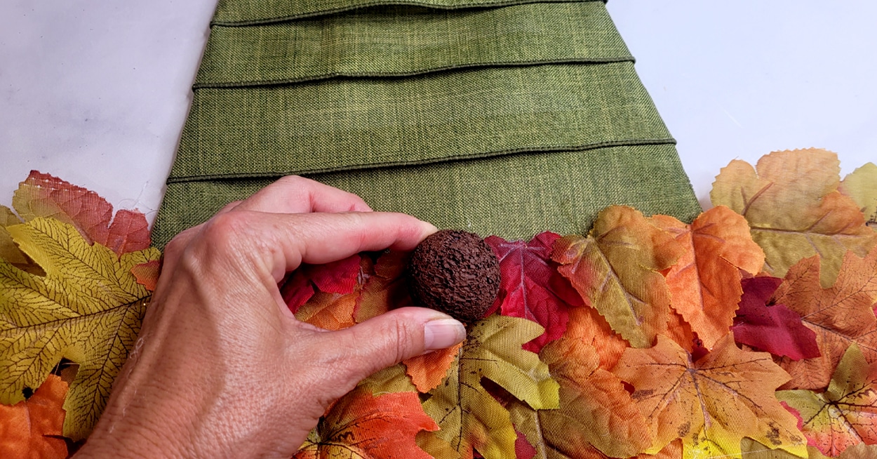 A hand holding a brown ball with green ribbon and leaves in the background.