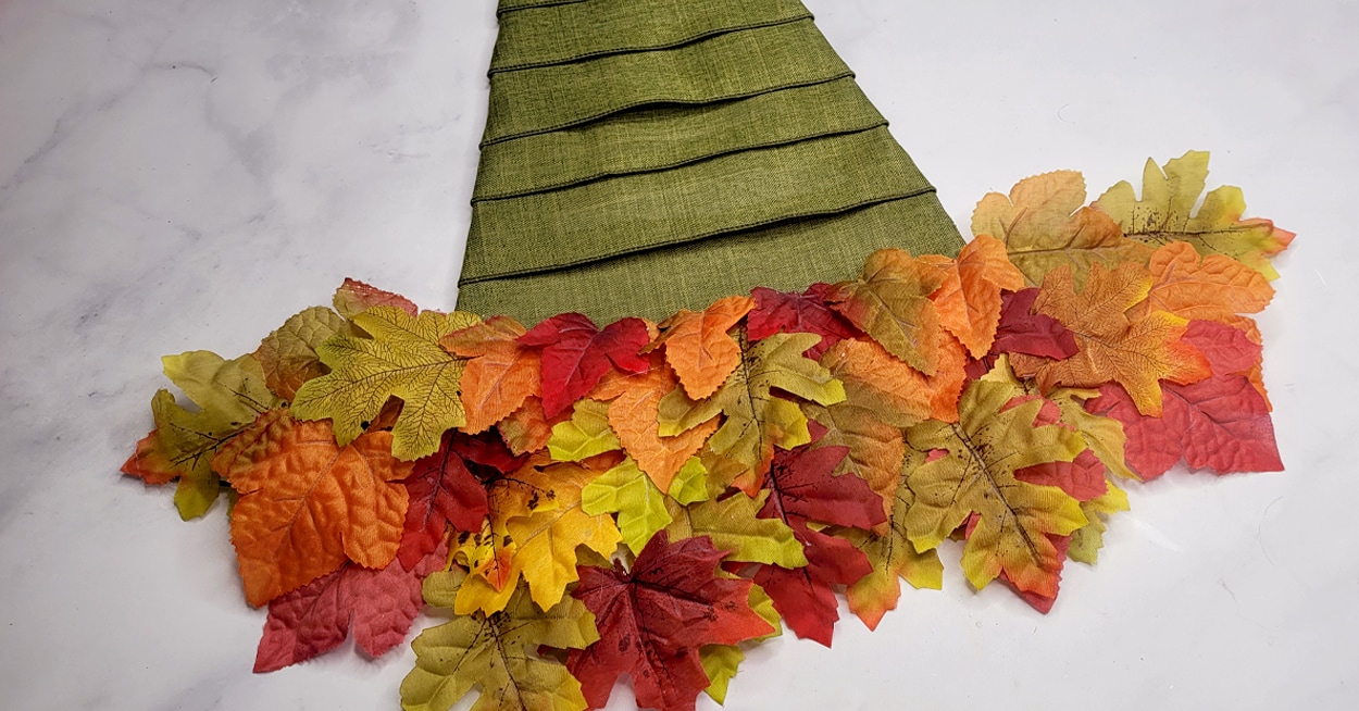 A wire wreath form with green ribbon and leaves on it.