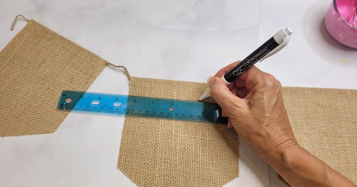 A burlap banner with a ruler on it and a hand holding a pen.