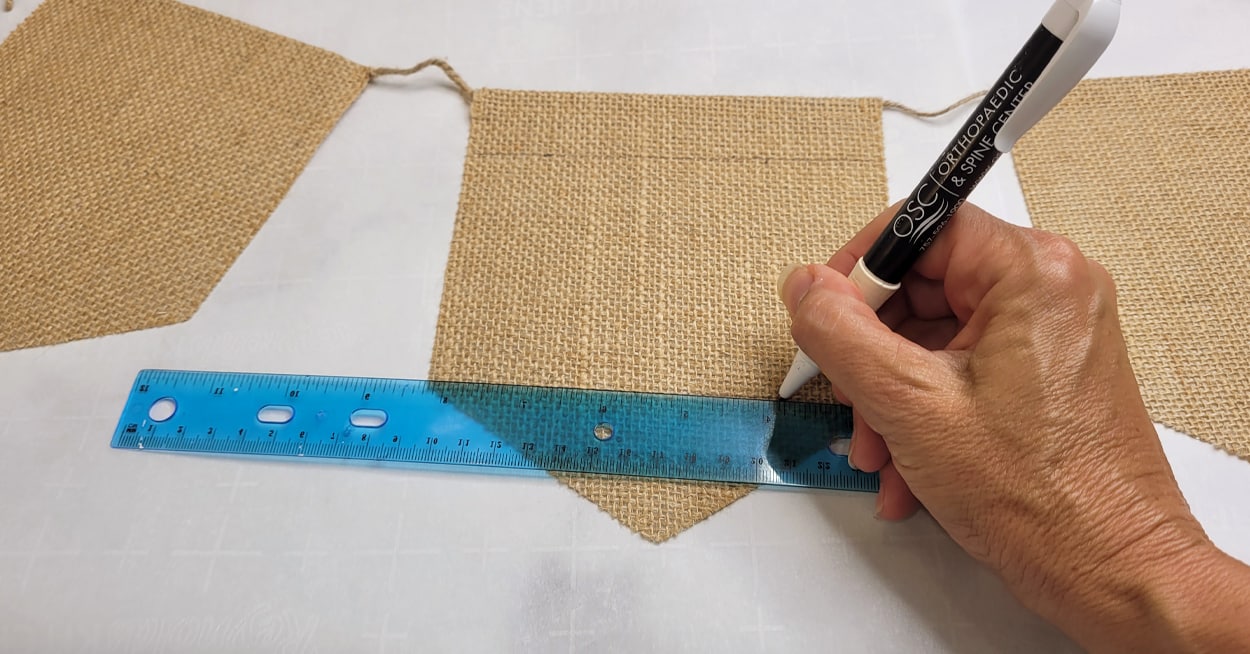 A burlap banner with a ruler on it and a hand holding a pen.