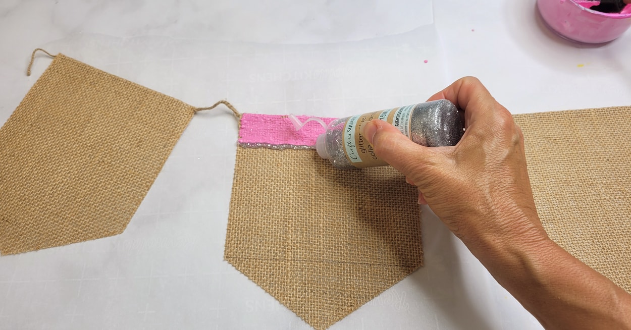 A burlap banner with a line of pink paint on it and a hand holding a ...