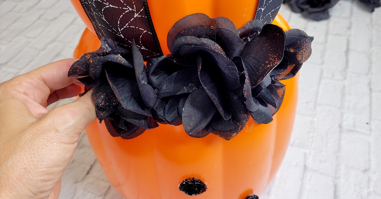 A hand holding black flowers on stackable pumpkins.