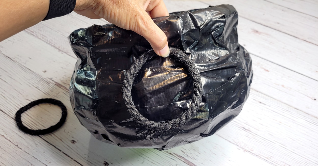 A hand holding a black pot with big handles on it.