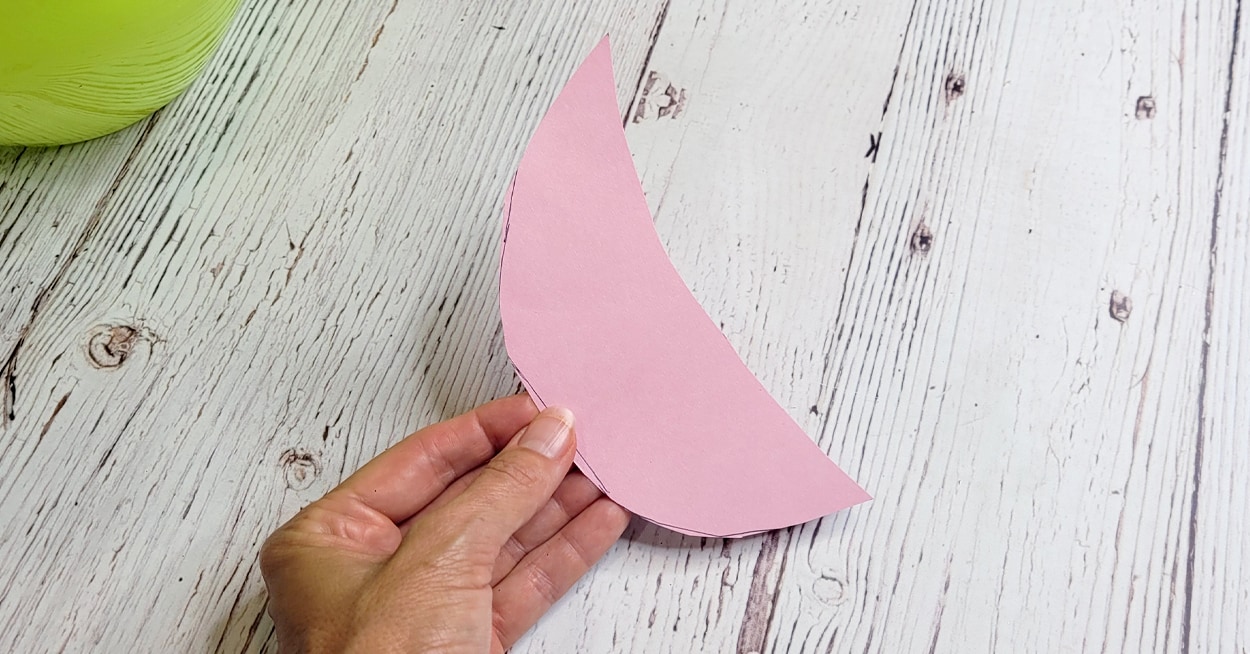 A hand holding a moon-shaped piece of pink paper.