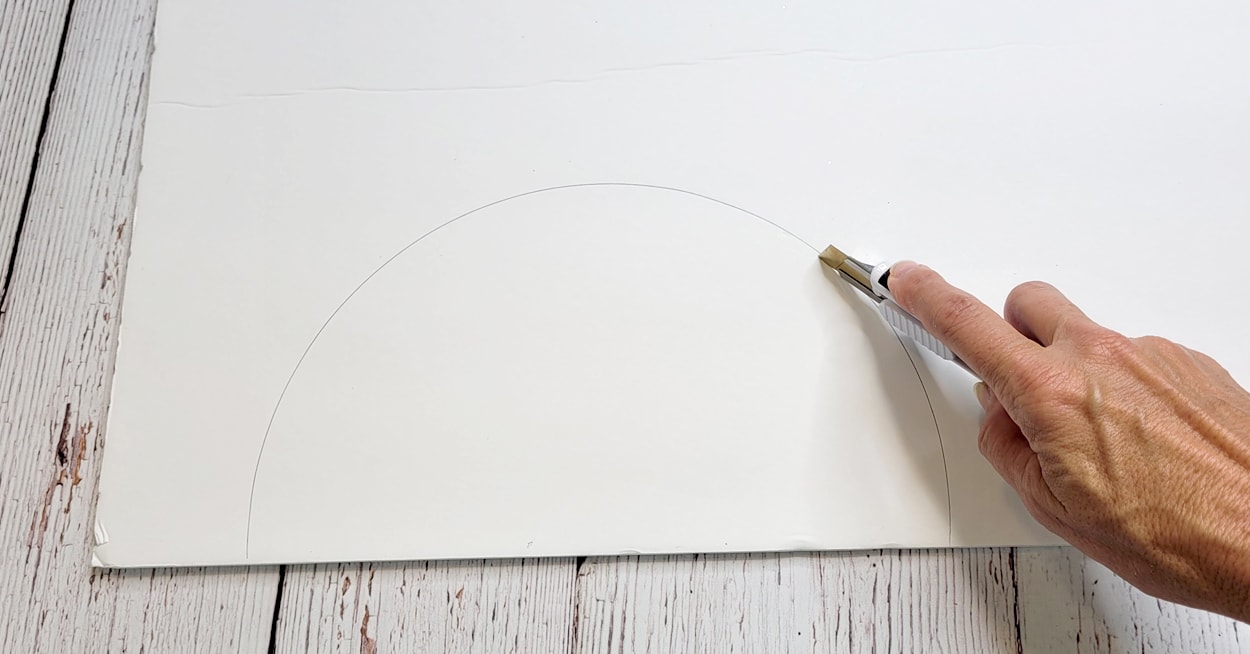 A hand holding a utility knife cutting a piece of white foam board.