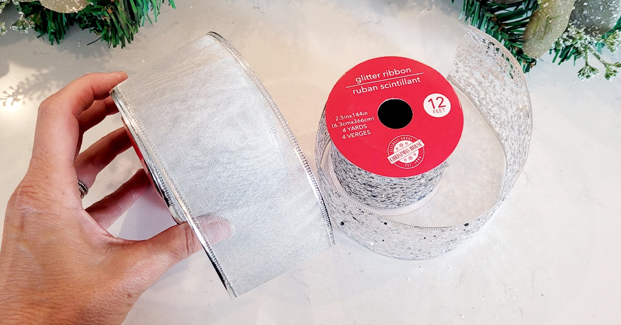 A hand holding a roll of silver ribbon and another roll of ribbon in ...