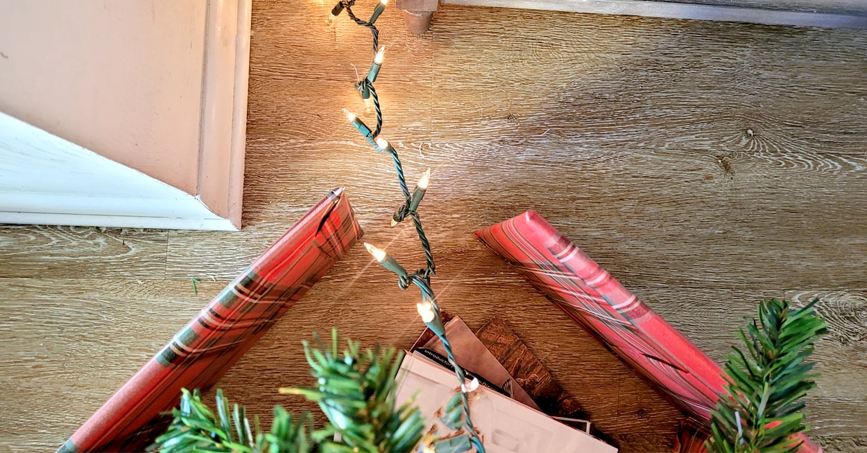 A plaid tree collar with a stand of white lights going through the opening.