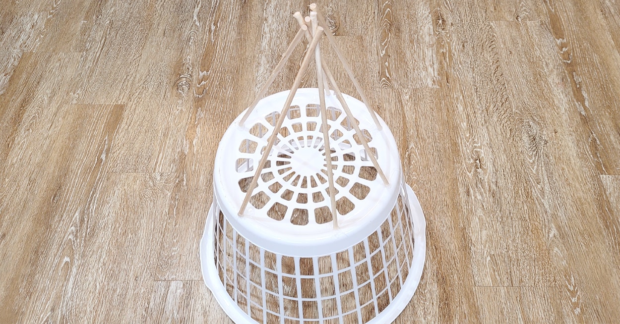 A white laundry basket with dowel rods forming a point on top.