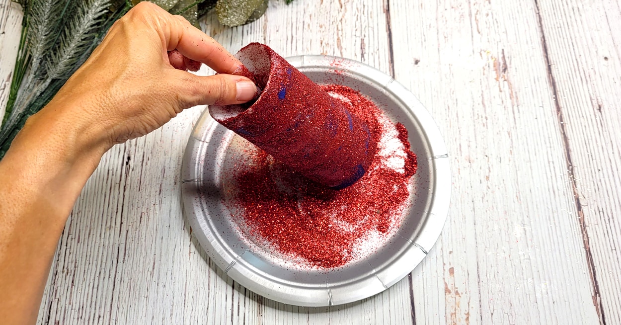 A hand holding a LED pillar candle that has red glitter all over it.