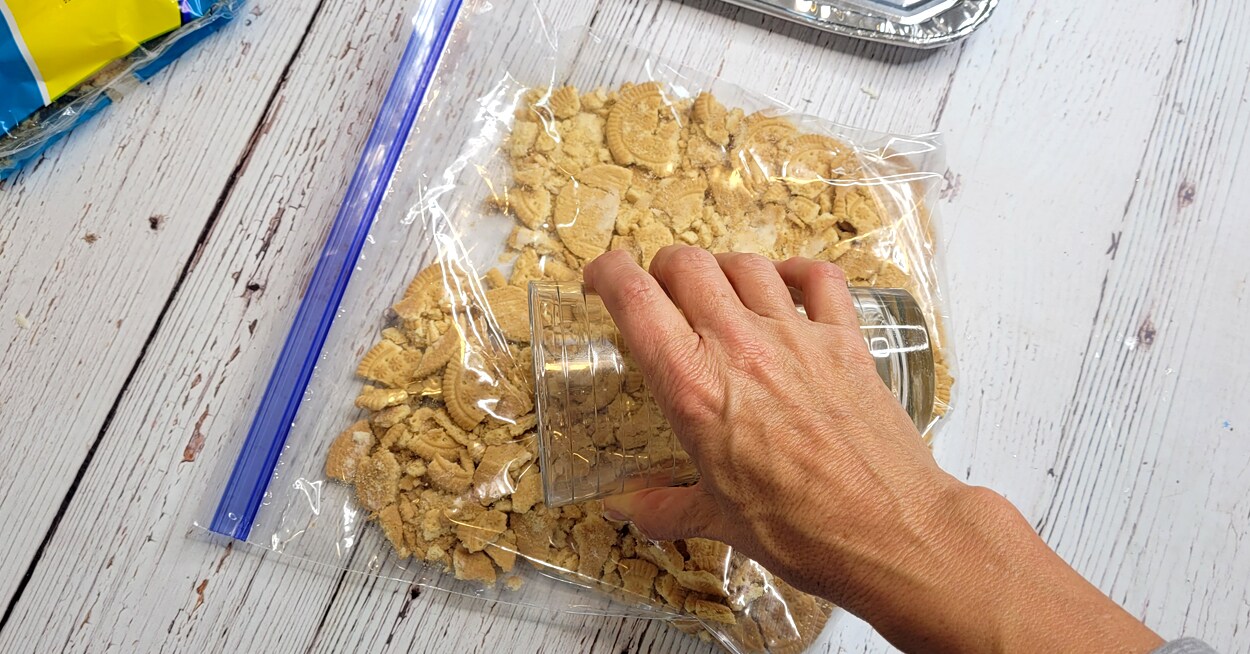 Hand holding a glass against a plastic bag filled with cookies to crush ...