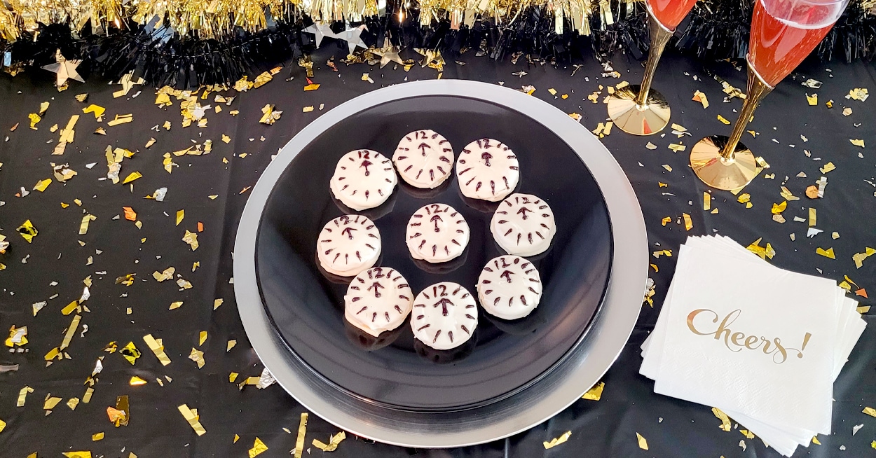 A black plate with white cookies with clock faces on them with confetti ...