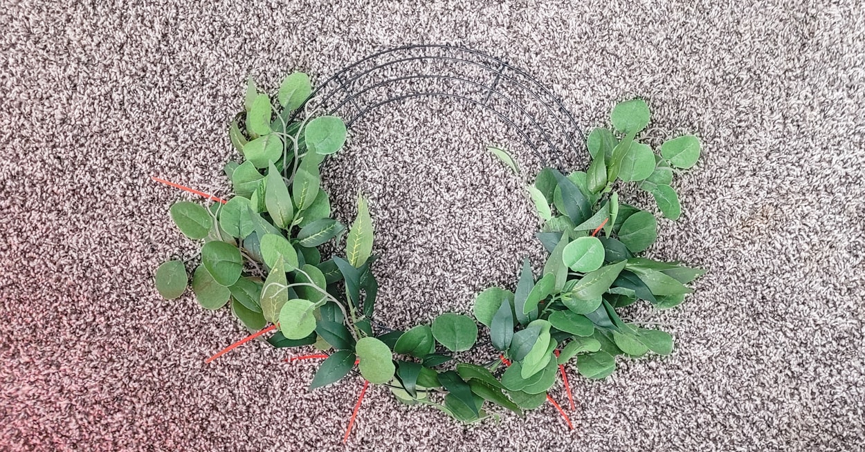 A round wire wreath form with some leaves on it.