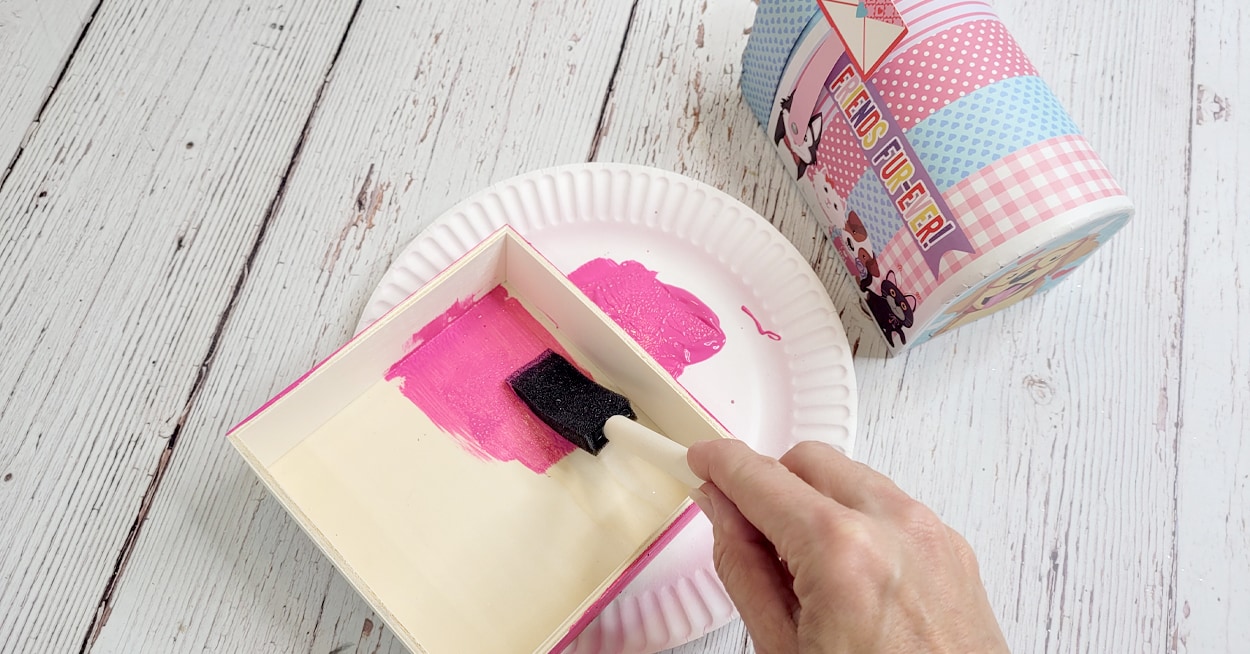 A hand painting a wooden box pink.