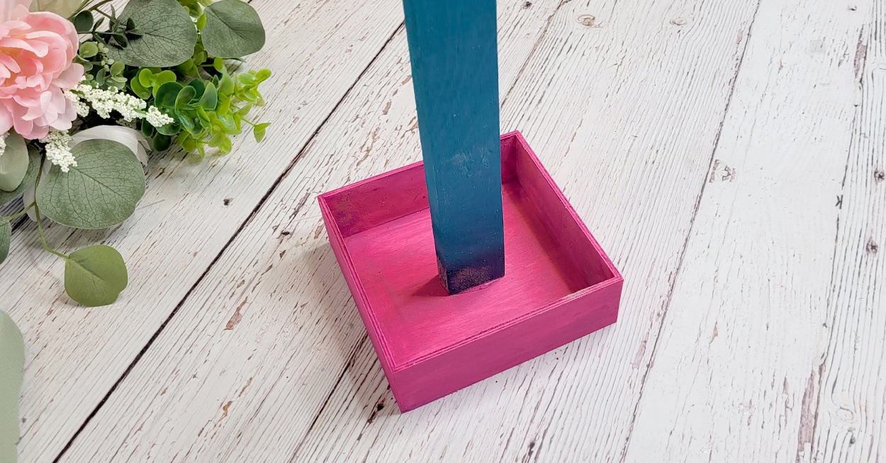 A piece of blue wood standing in a pink box.