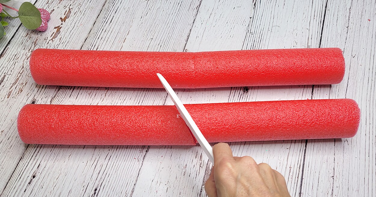 A hand holding a pool noodle knife cutting a red pool noodle.