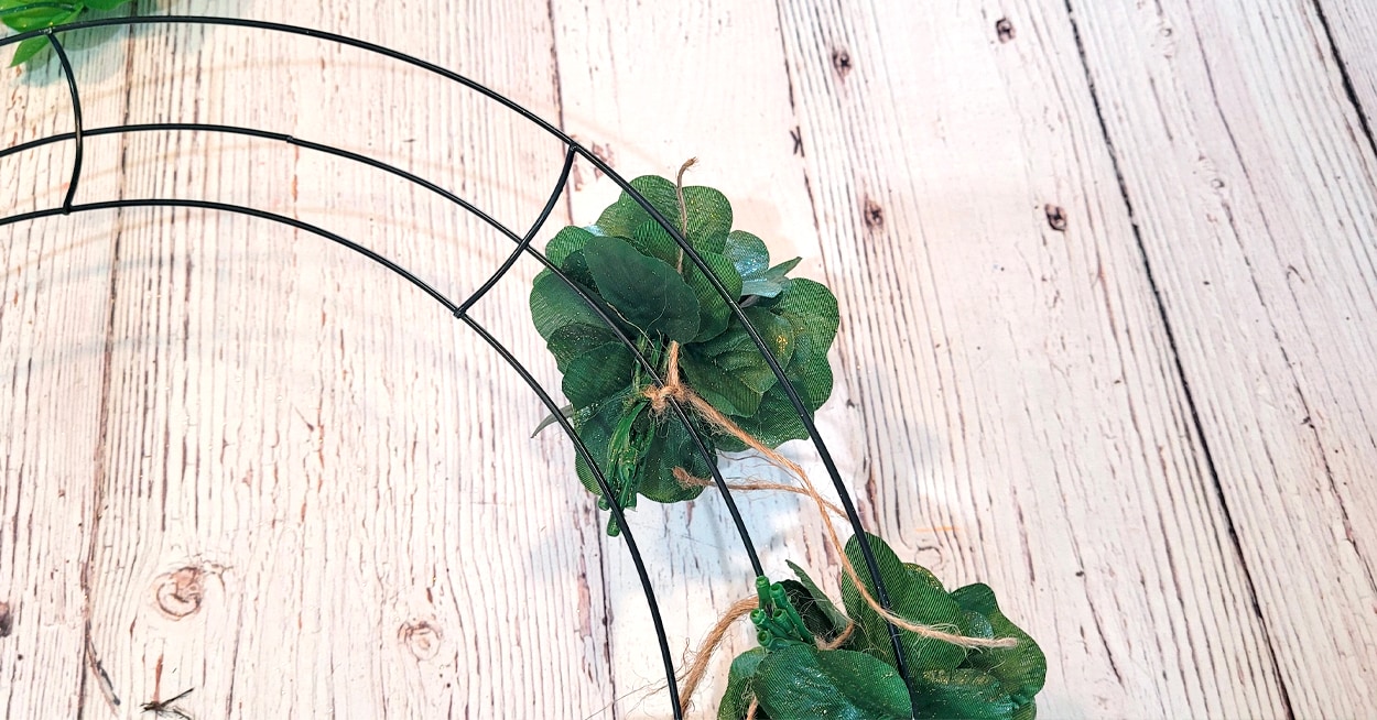 A wire wreath form with a bunch of green clovers tied to it with twine.