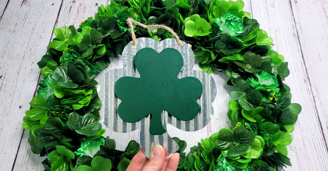 A green clover wreath with a hand holding a larger metal clover.