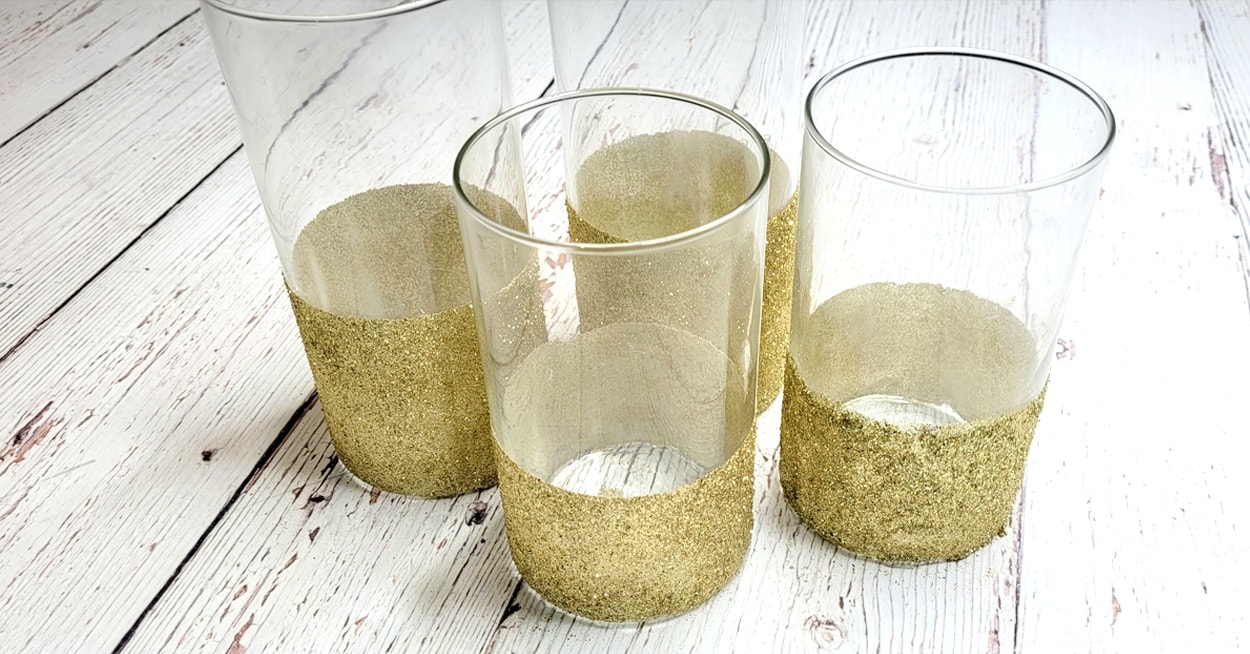 4 glass cylinder vases with gold glitter on the bottom halves.
