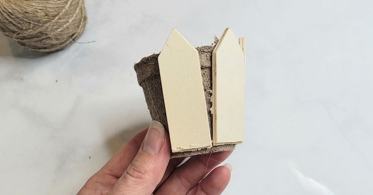 A hand holding a small piece of wood on a small brown pot.